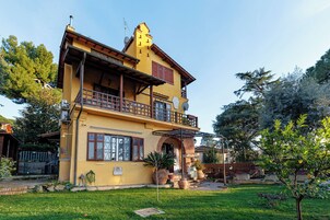 Uma casa de dois andares com varanda, um pequeno jardim e céu claro.