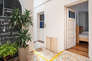 Um corredor com planta em vaso, piso de azulejos, radiador e porta que dá para um quarto.