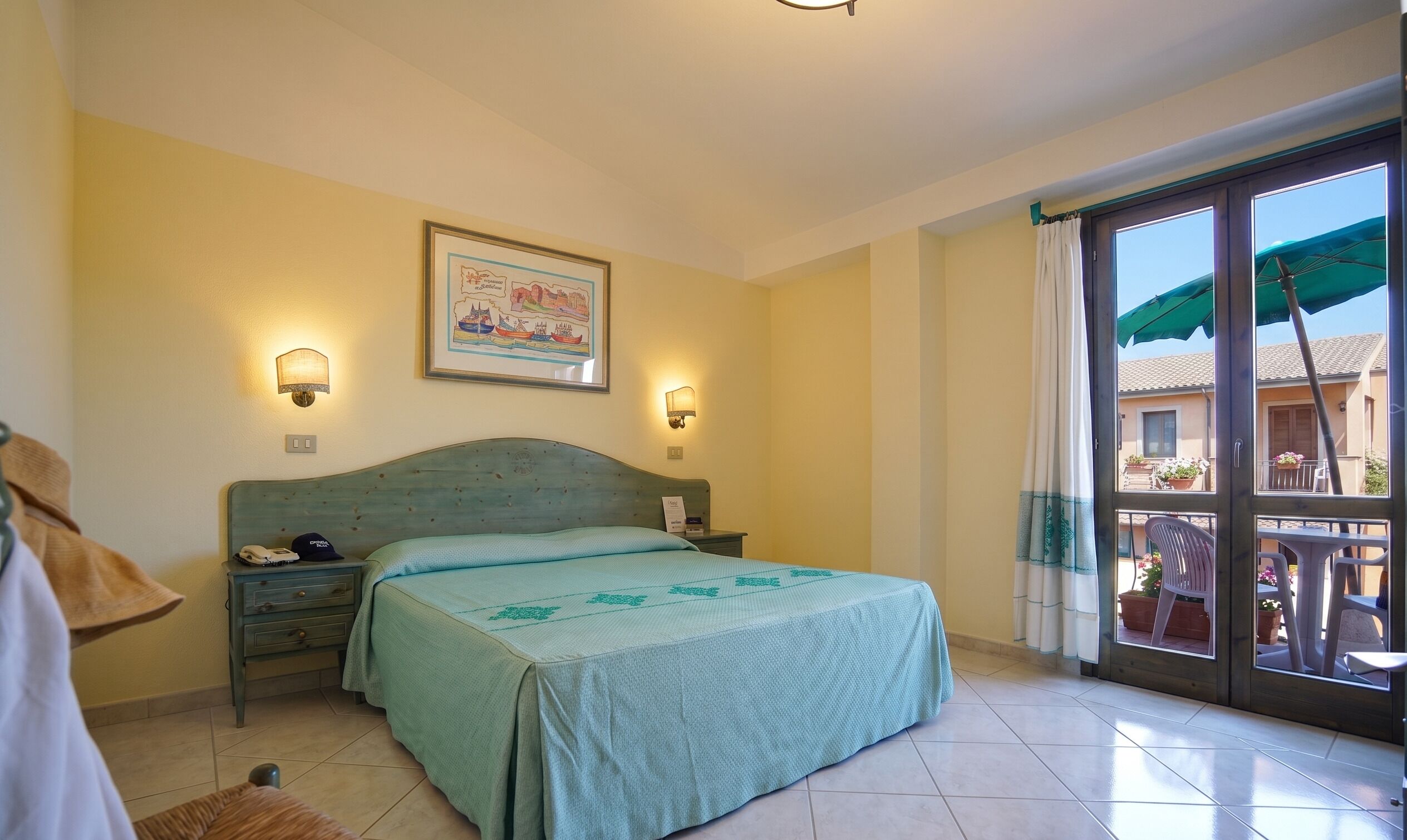 Quarto com cama, duas luminárias na parede, um mapa emoldurado e varanda com vista para o exterior.