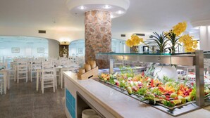 Uma área de buffet com um pilar de pedra, uma vitrine de vidro e uma variedade de frutas e legumes.