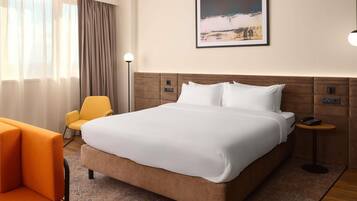 Quarto de hotel com uma cama grande, uma cadeira, uma mesa de cabeceira com telefone e um quadro na parede.