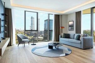 Uma sala de estar moderna com vista para a cidade, um sofá, uma poltrona, uma mesa de centro e uma televisão.