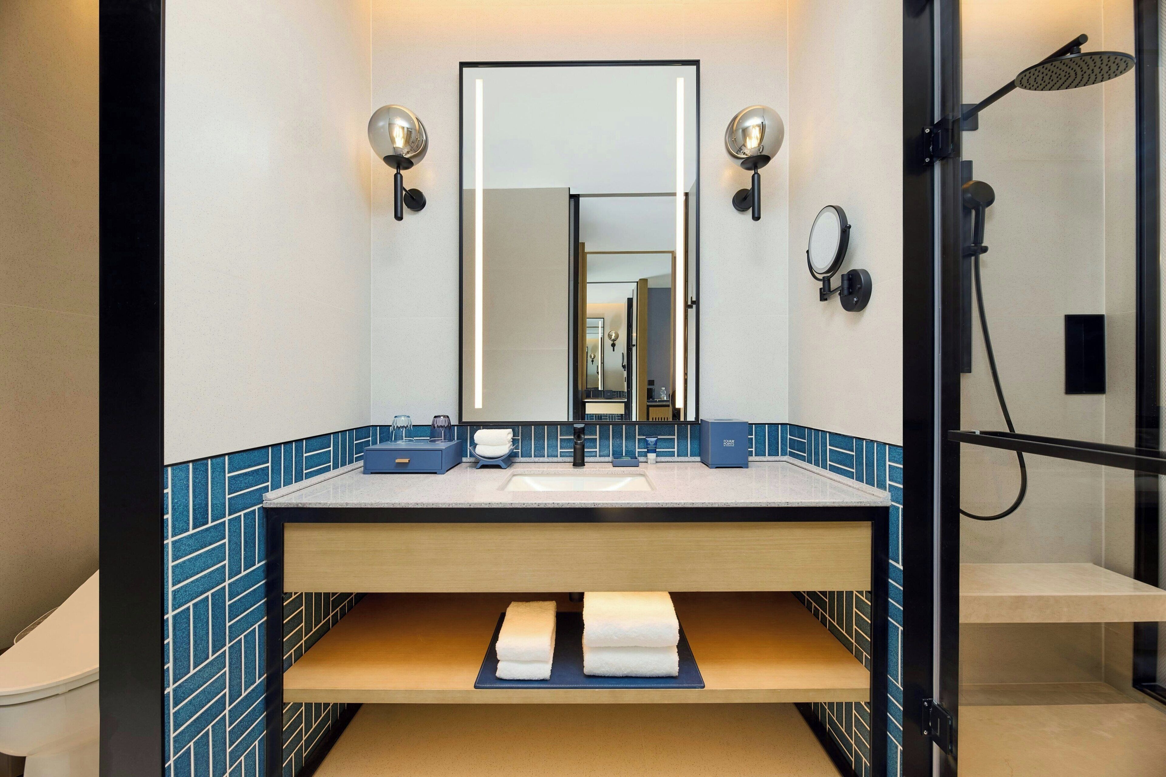 Casa de banho moderna com um espelho grande, duas luzes embutidas, um chuveiro manual e um porta-toalhas.