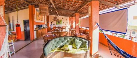 Um espaço interno amplo com teto alto, móveis de vime e uma rede.
