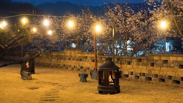 Área externa com paredes de pedra, luzes de festa e duas estruturas em estilo lanterna.