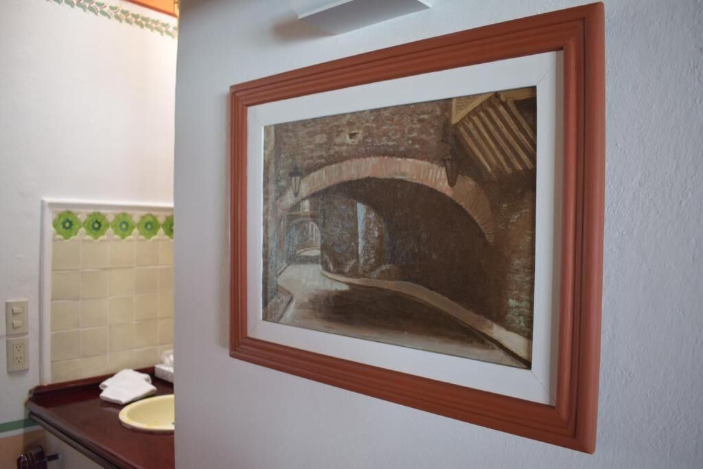 Pintura emoldurada de uma ponte de pedra arqueada em um banheiro com pia branca e toalha no balcão.
