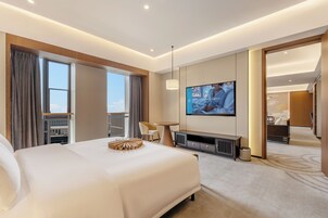 Quarto de hotel com cama grande, televisão, escrivaninha e vista para a cidade.