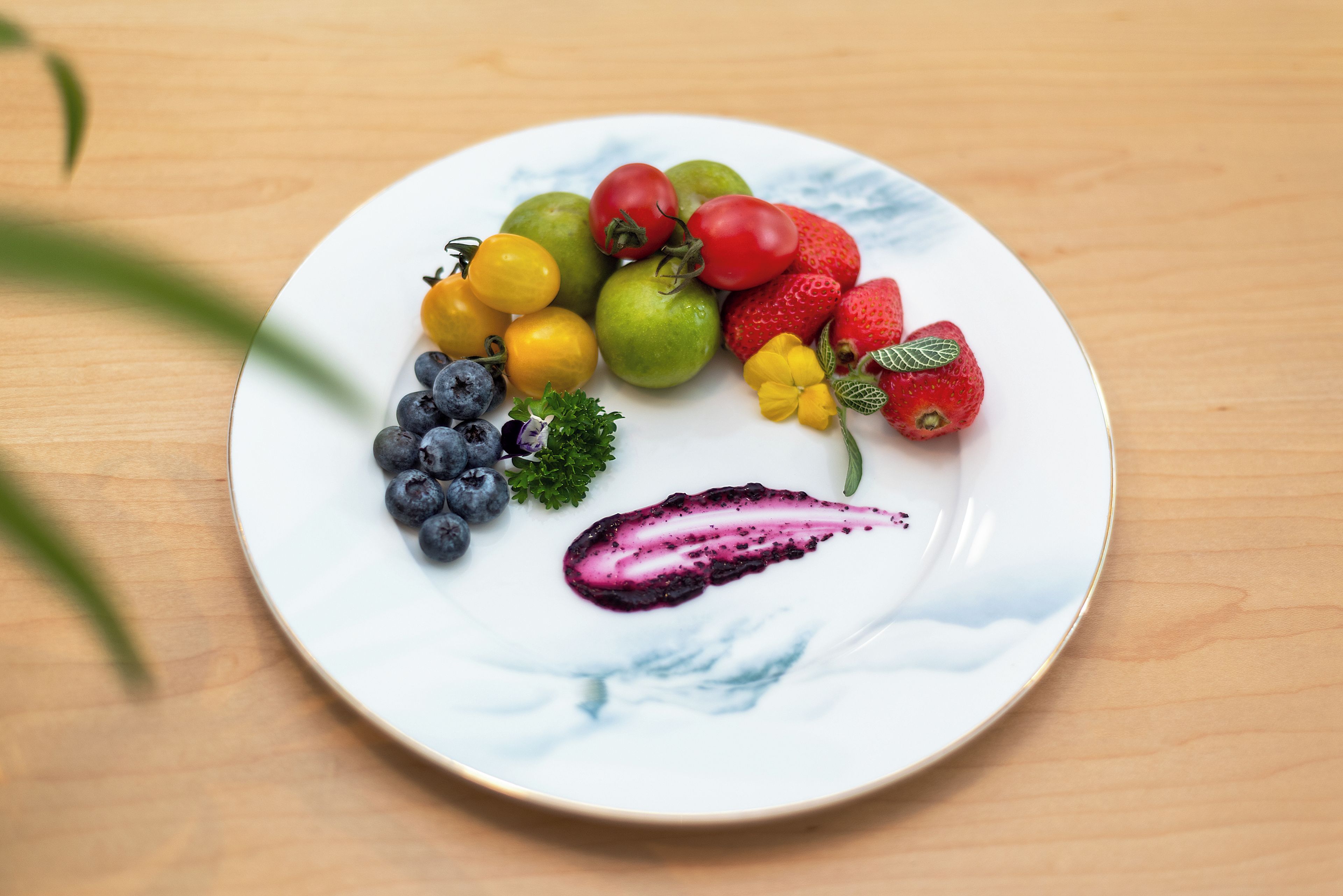 Prato com diversas frutas e um molho de bagas sobre uma mesa de madeira.