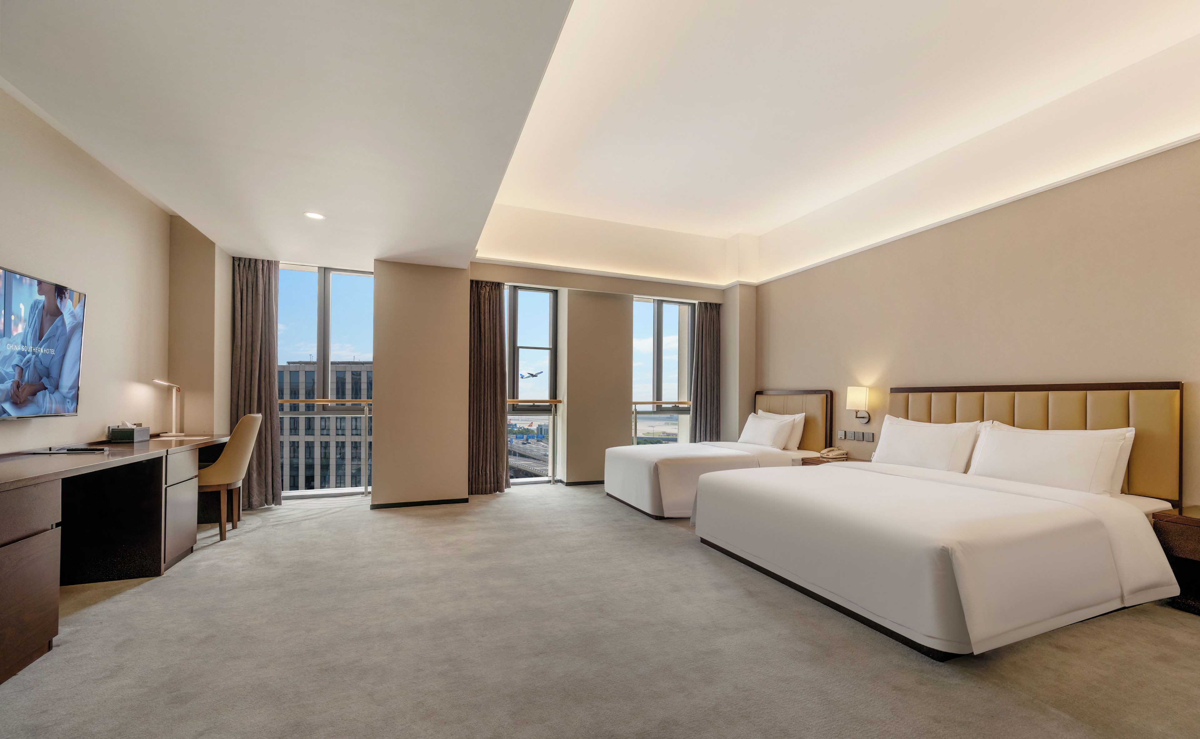 Quarto de hotel com escrivaninha, duas camas, televisão e vista para a cidade.
