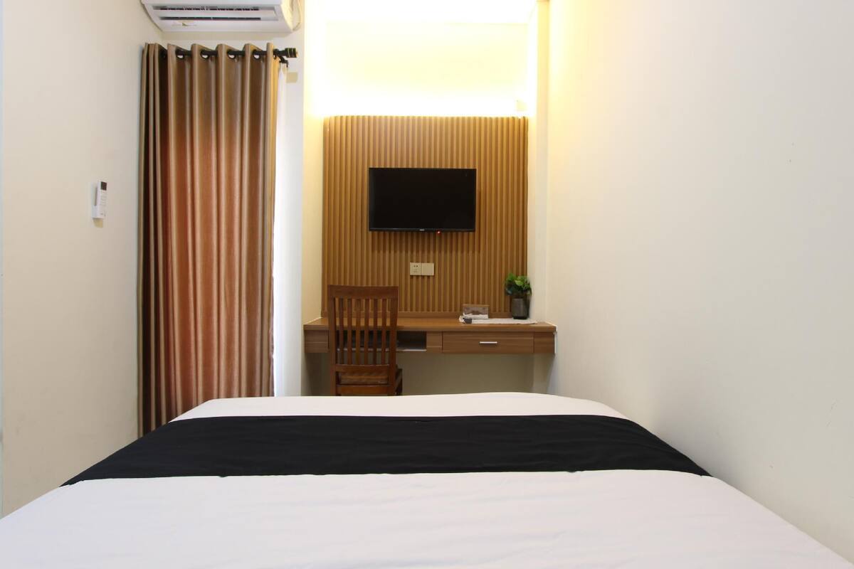 Quarto de hotel com cama, escrivaninha, cadeira, televisão e cortina.