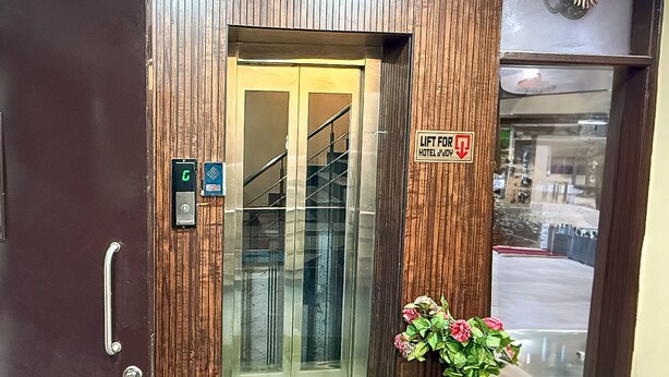 Entrada de hotel com fachada de madeira, elevador para hóspedes e porta de vidro.