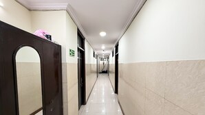 Um corredor longo e estreito, com uma porta escura à esquerda e um sinal de saída de incêndio acima.