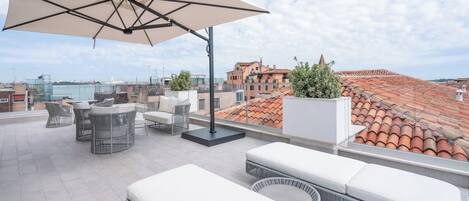 Terraço no telhado com mobiliário externo, um grande guarda-sol e vista para o horizonte da cidade.