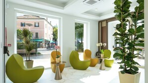 Um hall moderno com cadeiras verdes e amarelas, piso de mármore e grandes janelas com vista para a rua.