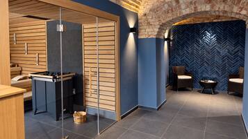 Uma área de spa moderna com sauna de madeira, mesa de massagem e espaço de estar com móveis de vime.