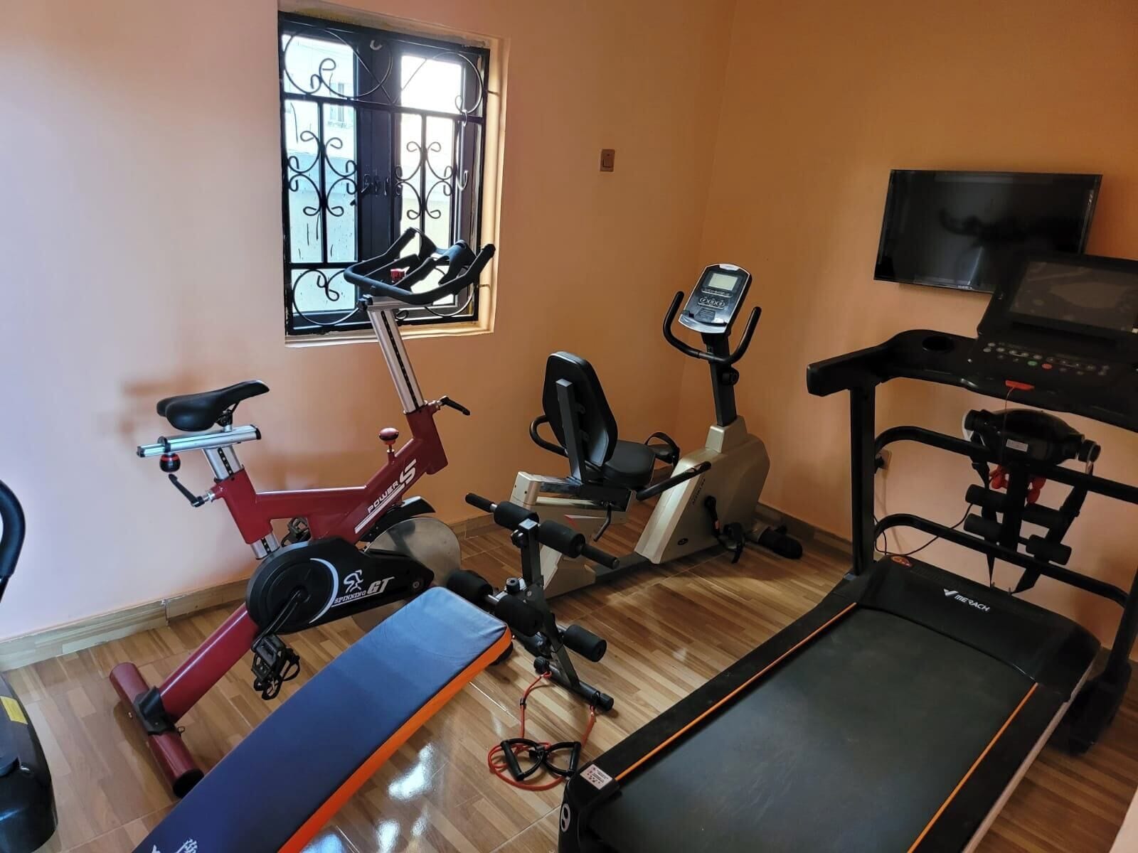 Uma academia em casa com bicicleta ergométrica, elíptico, esteira e um banco.