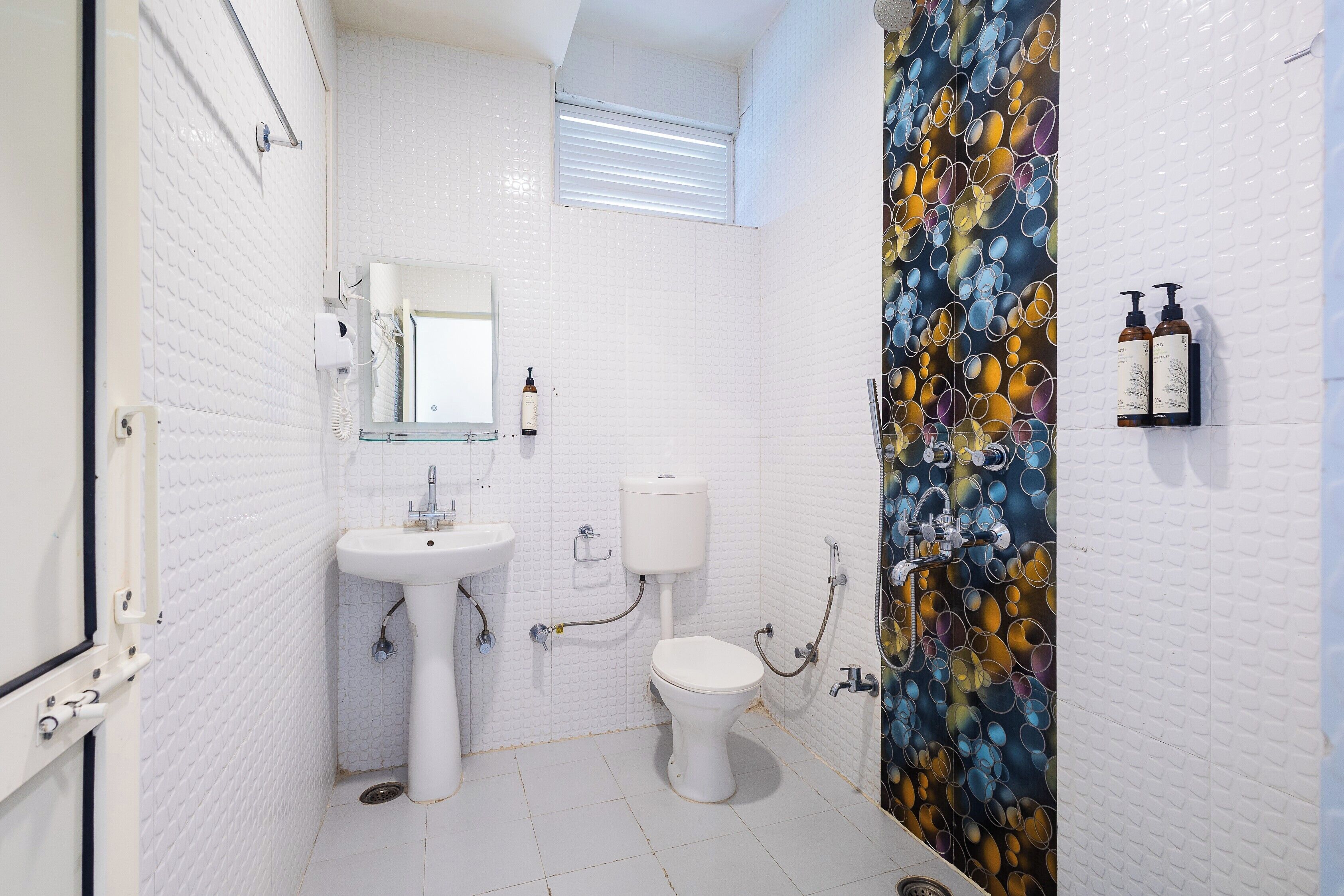 Um banheiro com parede de azulejos brancos, pia, vaso sanitário e cortina de chuveiro com padrão circular.