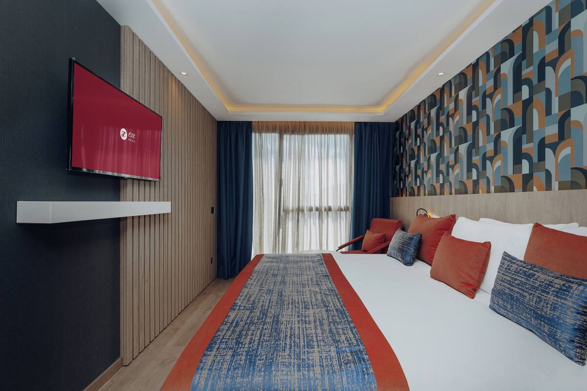 Quarto de hotel moderno com uma cama grande, uma TV de tela plana na parede e um papel de parede estampado.
