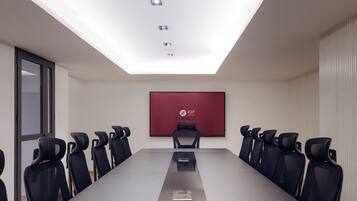 Uma sala de conferências com uma mesa comprida, cadeiras pretas, um logotipo vermelho na parede e uma clarabóia.
