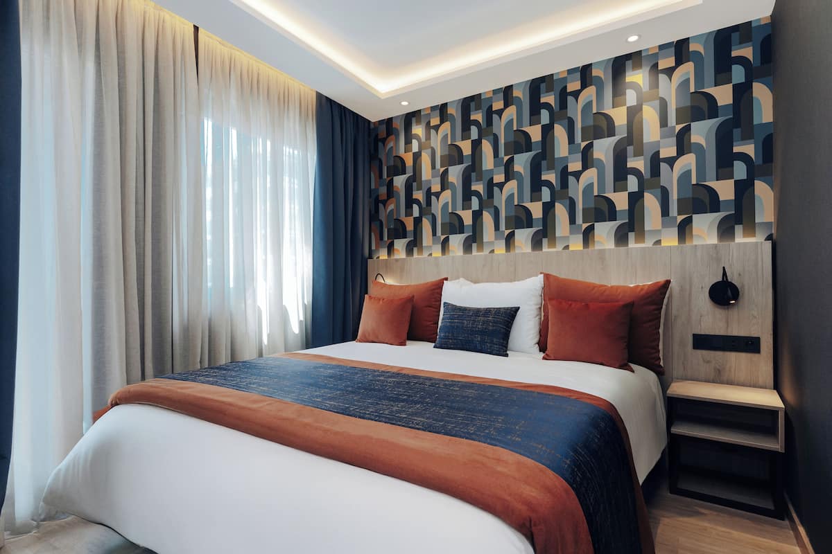Quarto de hotel moderno com uma cama grande, cabeceira de madeira e parede com padrão geométrico.