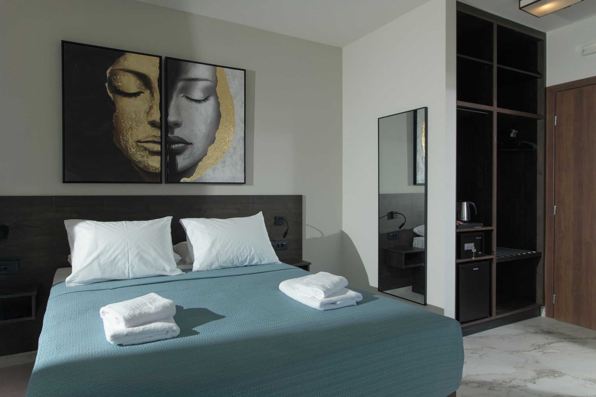 Quarto de hotel moderno com uma cama grande, um guarda-roupa, um espelho e um quadro na parede.