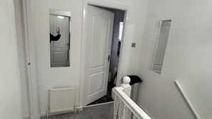 Uma escada estreita com corrimão branco, degraus carpetados e uma porta no topo.