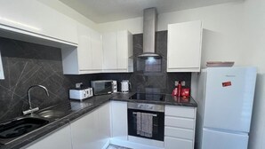 Uma cozinha moderna com armários brancos, bancada preta, forno embutido, micro-ondas e geladeira.