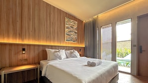 Quarto de hotel moderno com cabeceira de madeira, cama grande com roupa de cama branca, um banco e vista para o verde pela janela.
