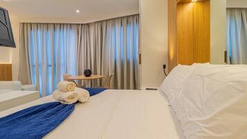 Quarto de hotel moderno com uma cama bem arrumada, uma toalha azul e uma pequena mesa redonda com um vaso.