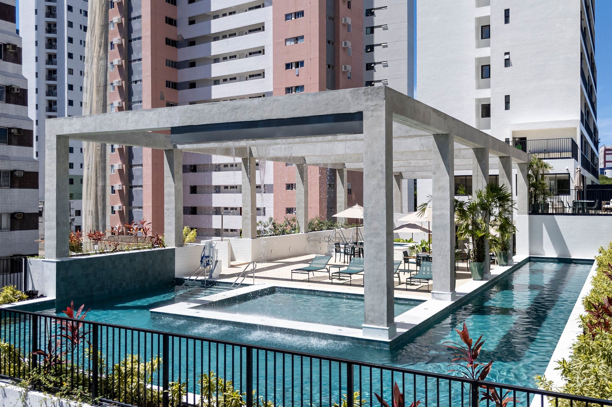 Uma área de piscina no terraço com um espaço de estar coberto, cercada por edifícios altos.