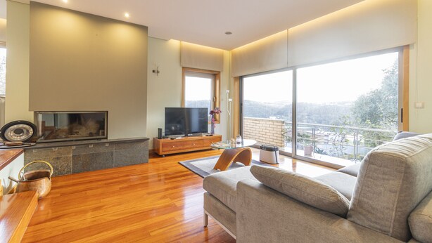 Uma sala de estar moderna com lareira, televisão de tela plana e uma grande janela com vista para a cidade.