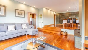 Uma sala de estar moderna com um sofá cinzento, uma mesa de centro de vidro e uma área de jantar com móveis de madeira.