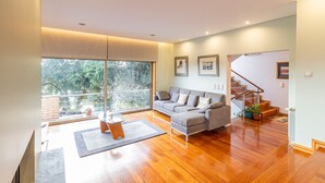 Uma sala de estar moderna com um sofá cinzento, piso de madeira e uma escada que leva a um andar superior.