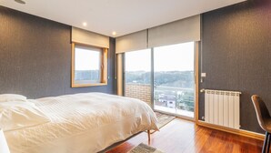 Quarto com uma cama grande, janela e vista para a paisagem urbana.
