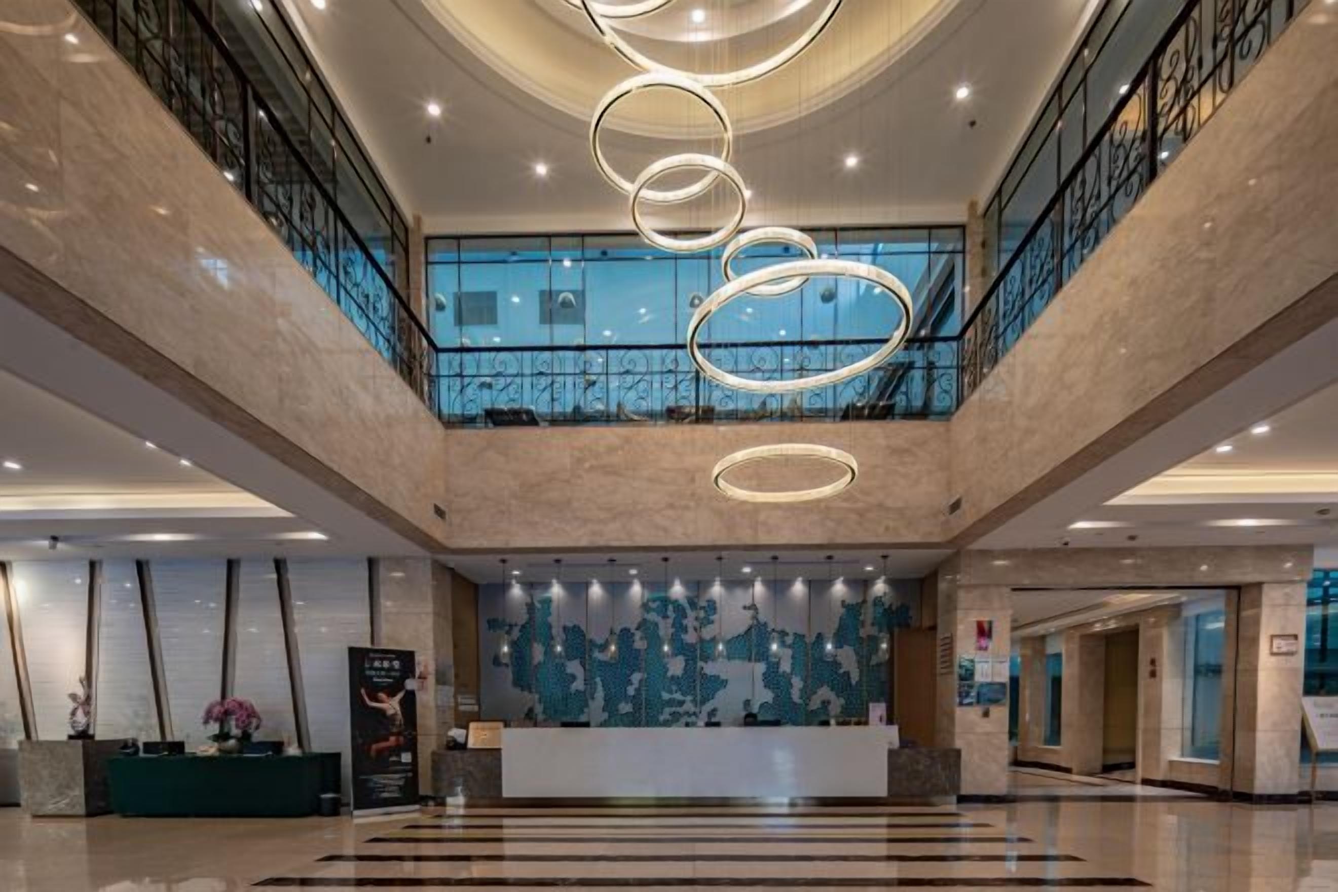 Um saguão de hotel com uma mesa de recepção, uma escadaria e um lustre decorativo.