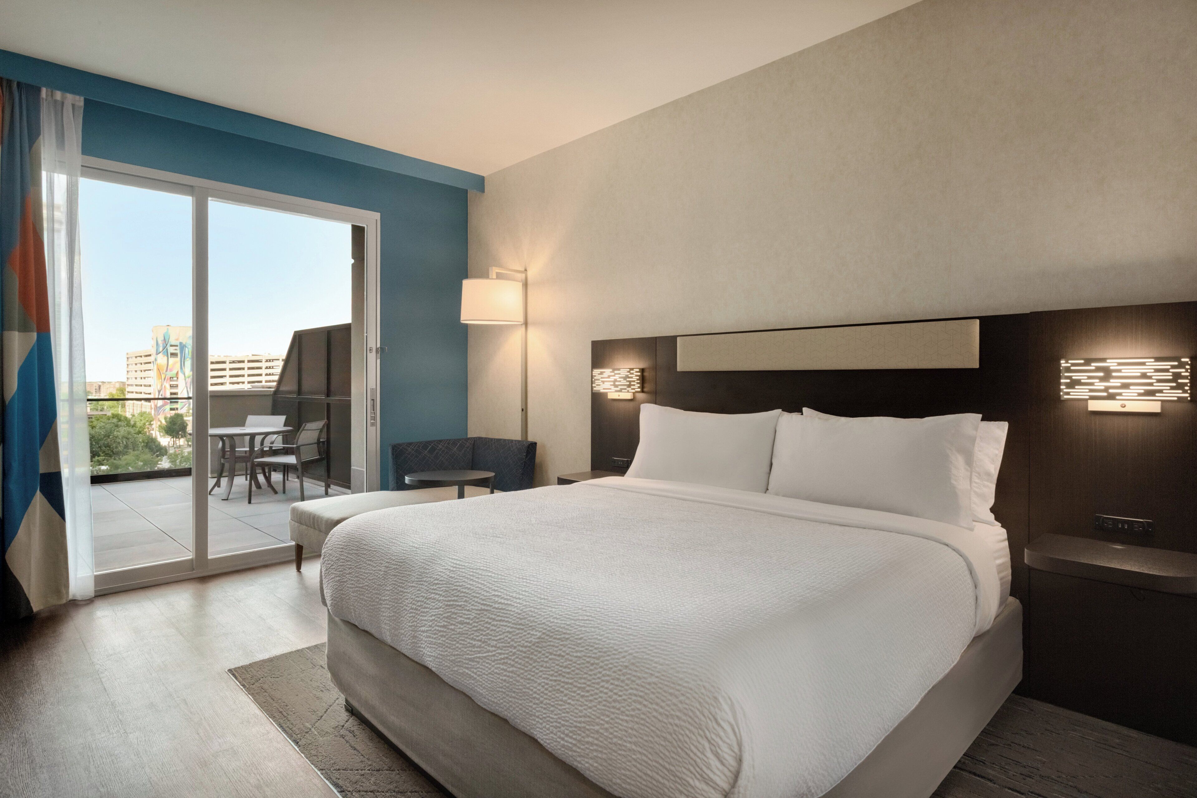Quarto de hotel com uma cama grande, uma escrivaninha e vista para a cidade pela janela.