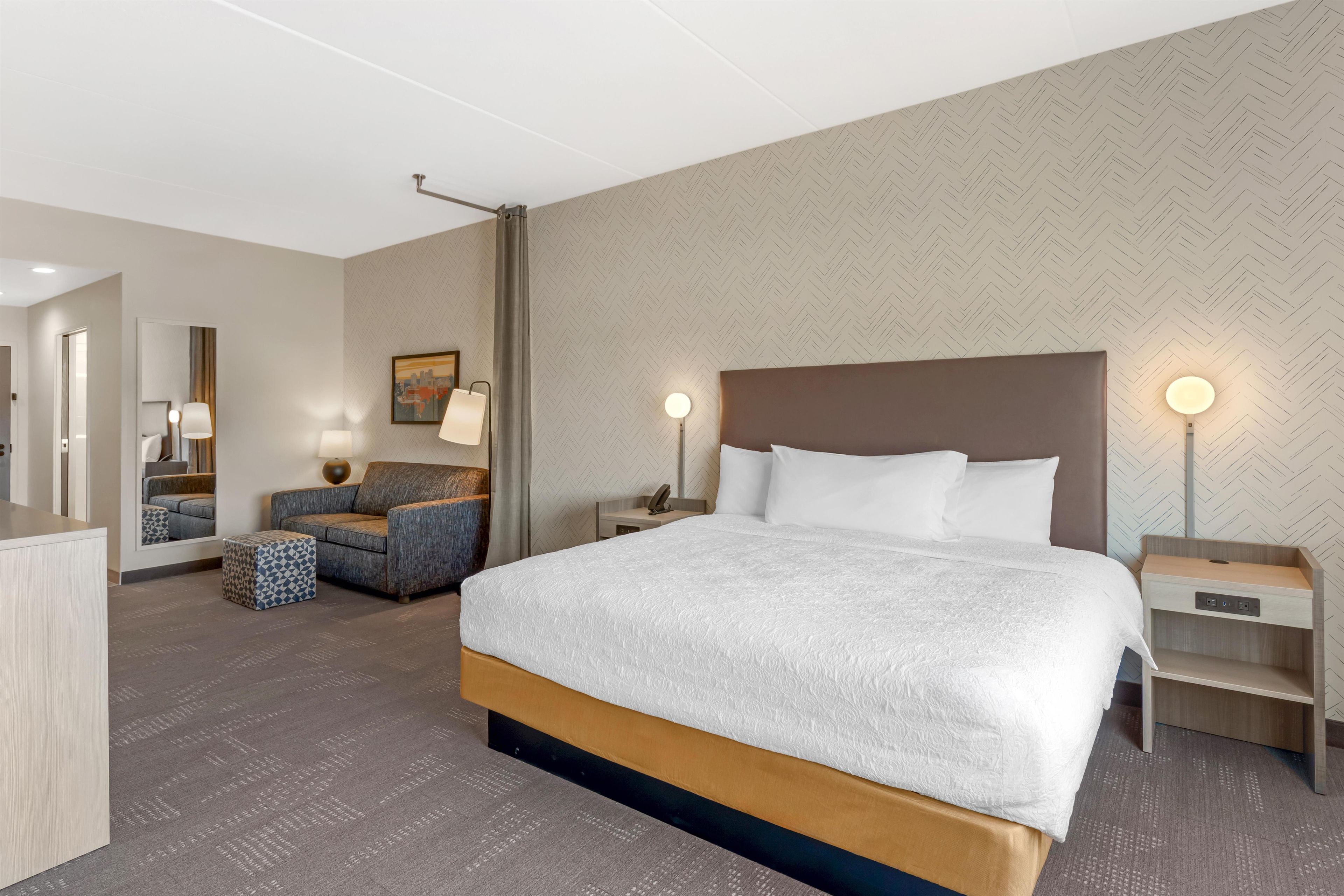 Quarto de hotel com uma cama grande, mesas de cabeceira, uma cadeira, escrivaninha e espelho.