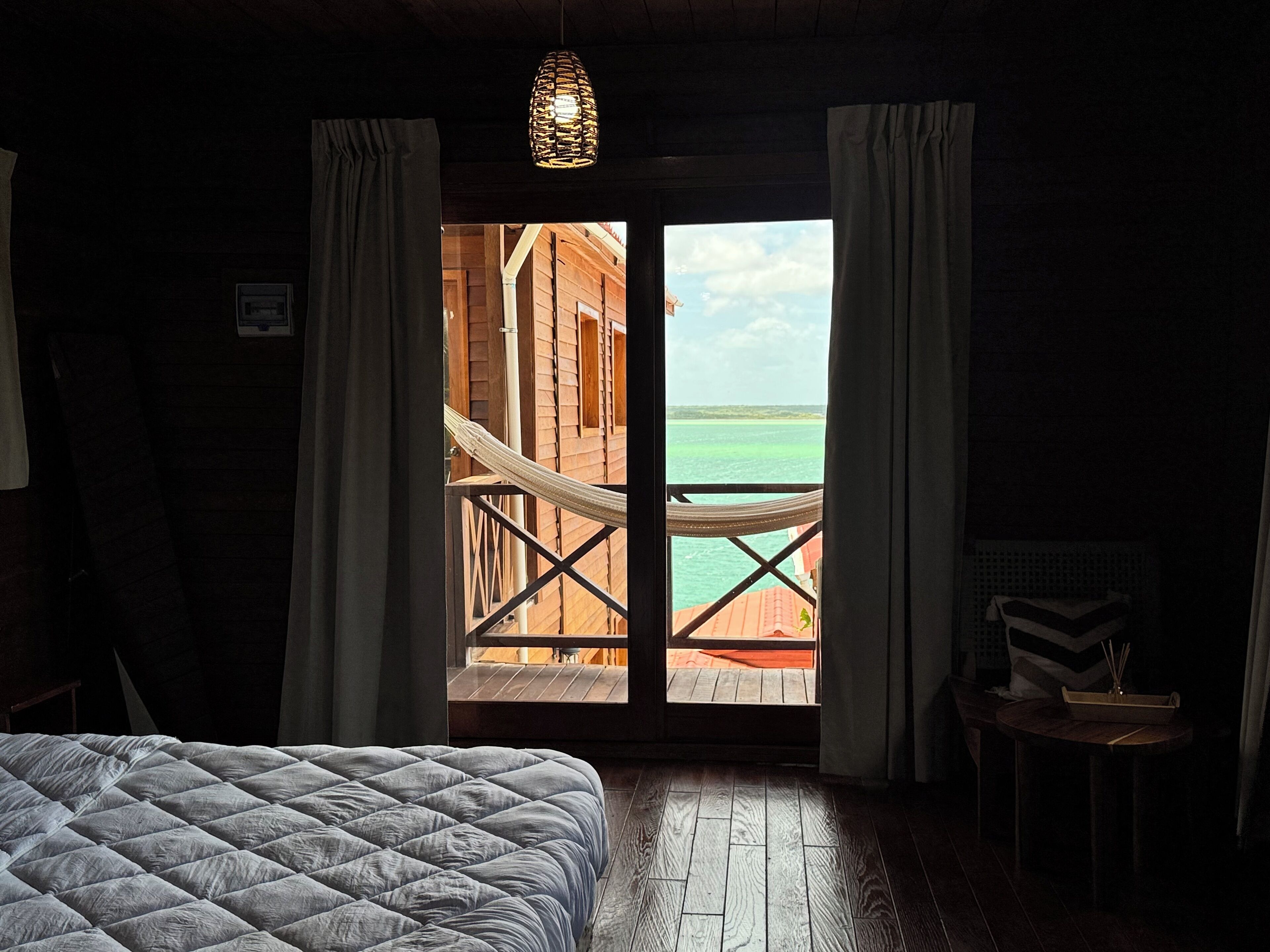 Quarto com cama, rede e vista para o oceano por uma porta de correr.