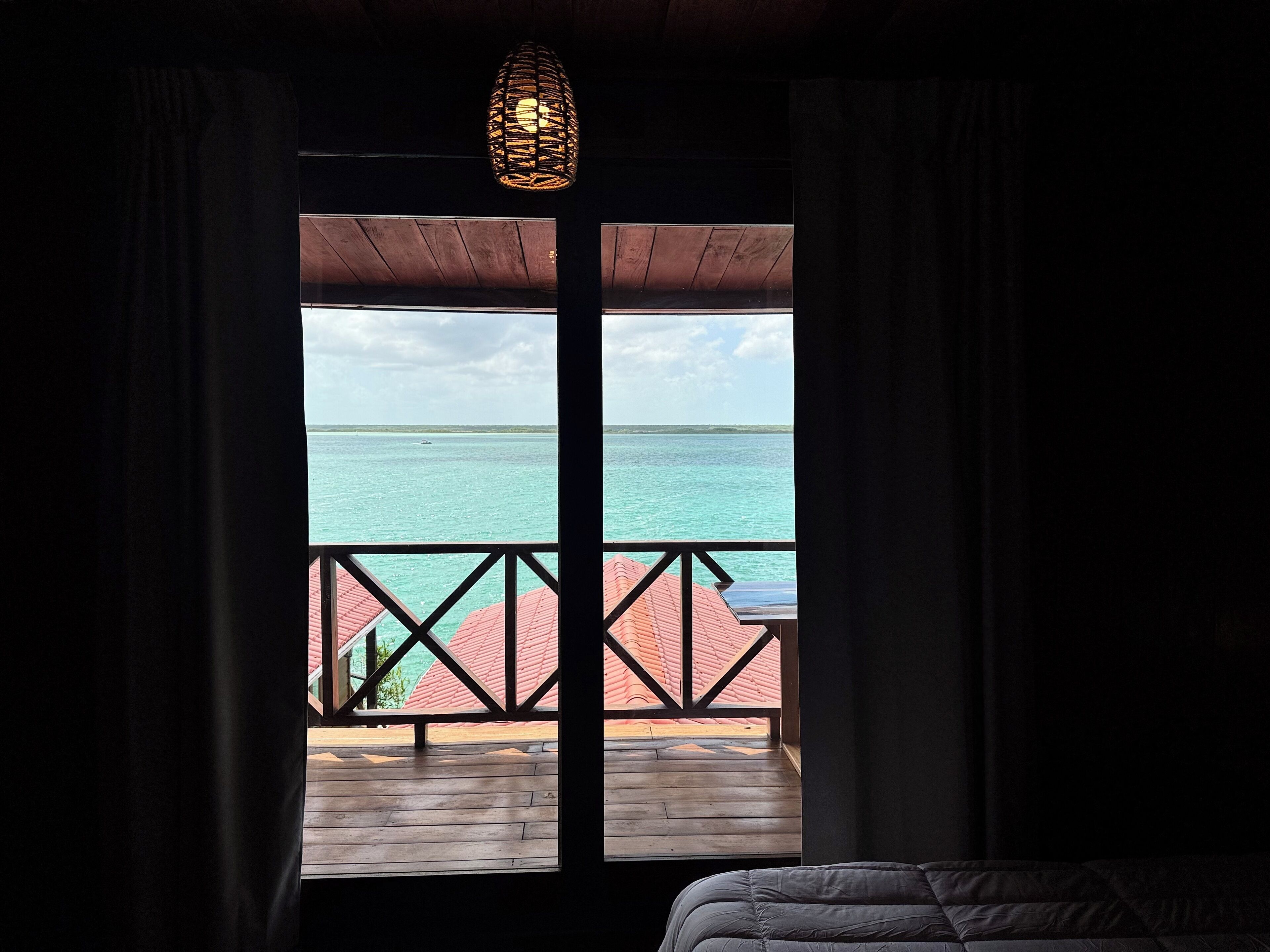 Quarto com uma janela grande de frente para a praia, piso de madeira e uma cama.