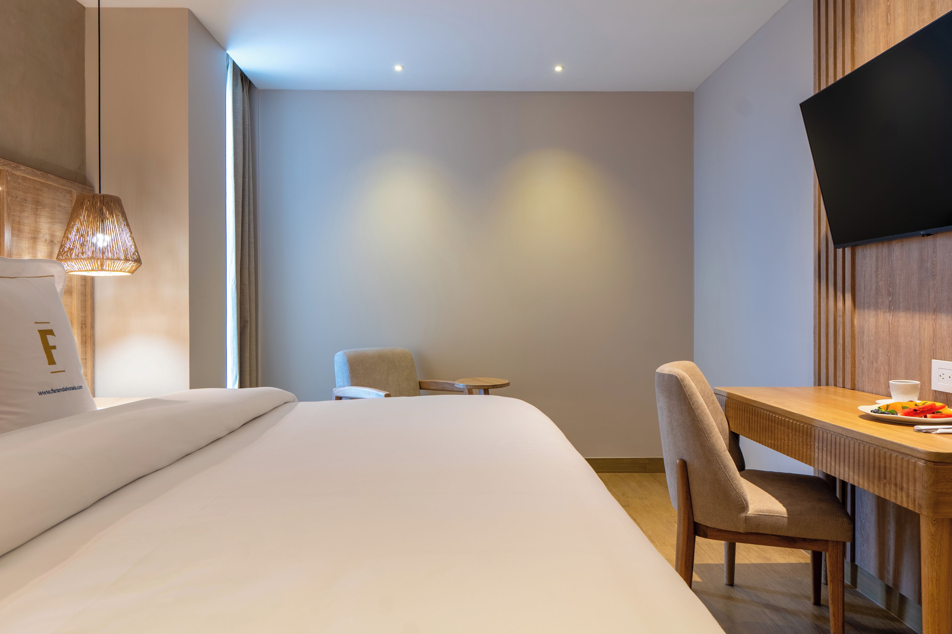 Quarto de hotel com cama, escrivaninha, cadeira, televisão e uma pequena mesa.