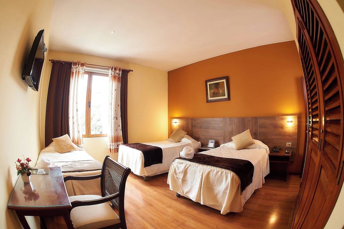 Quarto de hotel com duas camas, uma escrivaninha, uma cadeira, uma televisão e uma janela com cortinas.