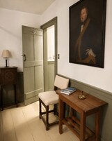Um quarto com uma escrivaninha de madeira, uma cadeira, um abajur, um retrato emoldurado e uma porta verde.