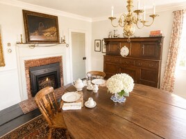 Uma sala de jantar com uma mesa de madeira posta para quatro pessoas, uma lareira, um lustre e um quadro grande na parede.