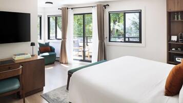 Quarto de hotel com cama, escrivaninha, cadeira, televisão e varanda com cortinas.