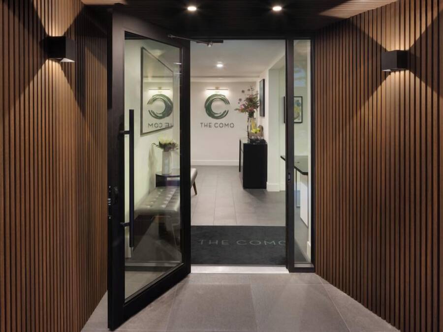 Entrada de um hotel moderno, com porta de vidro, balcão de recepção e placa na parede com a inscrição 'THE COMO'.