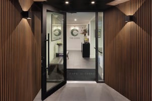 Entrada de um hotel moderno, com porta de vidro, balcão de recepção e placa na parede com a inscrição 'THE COMO'.