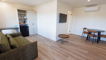 Uma sala de estar moderna com sofá, mesa de jantar com cadeiras, área de cozinha com armários e uma TV de tela plana fixada na parede.