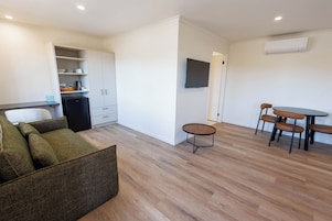 Uma sala de estar moderna com sofá, mesa de jantar com cadeiras, área de cozinha com armários e uma TV de tela plana fixada na parede.