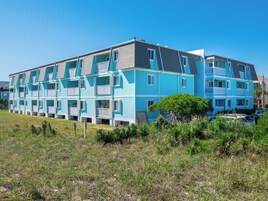 Um edifício residencial com várias andares, varandas, telhado plano e um gramado à frente.