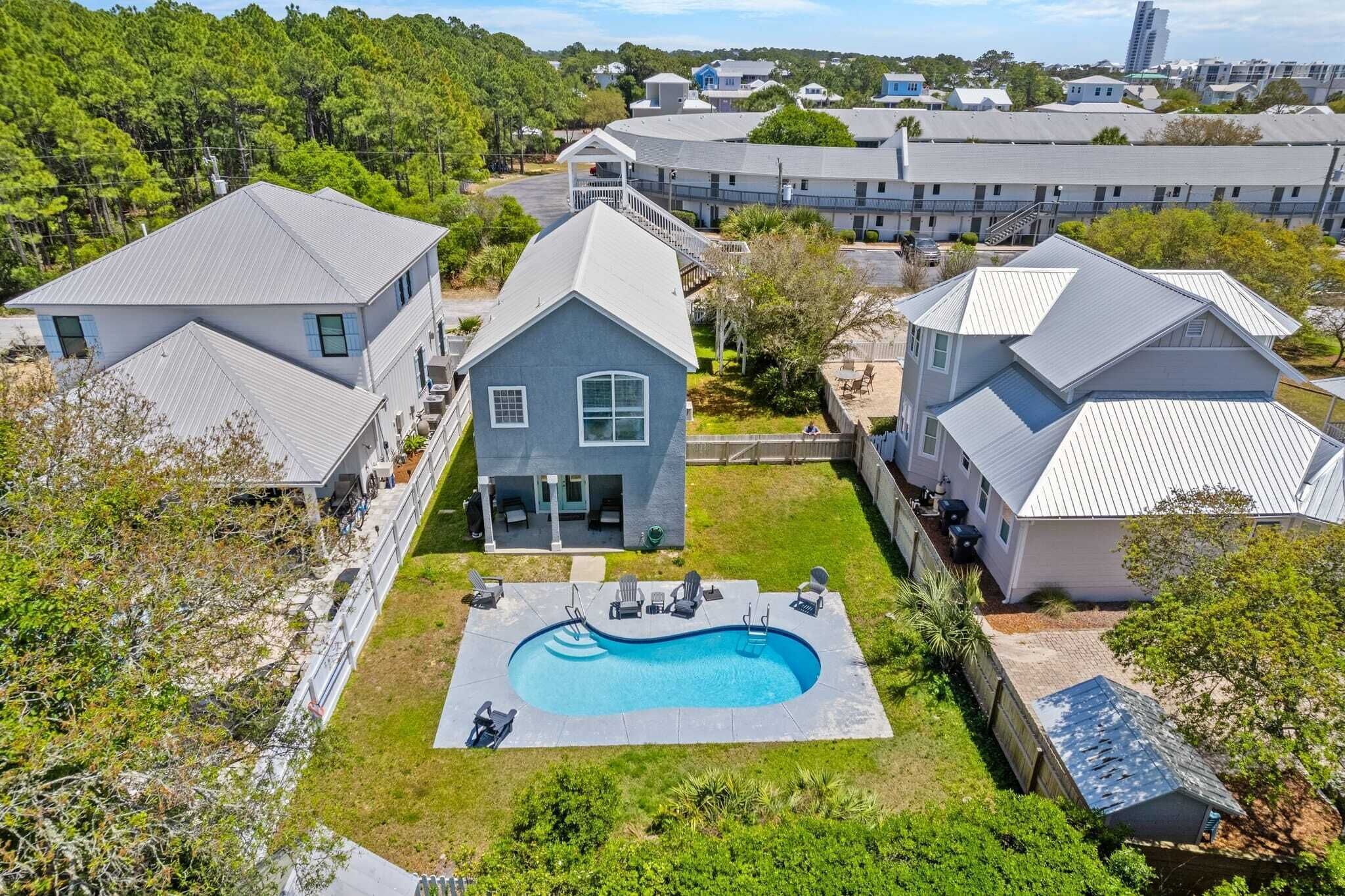Área residencial com piscina, rodeada por casas, um alpendre coberto e vista para uma área arborizada.